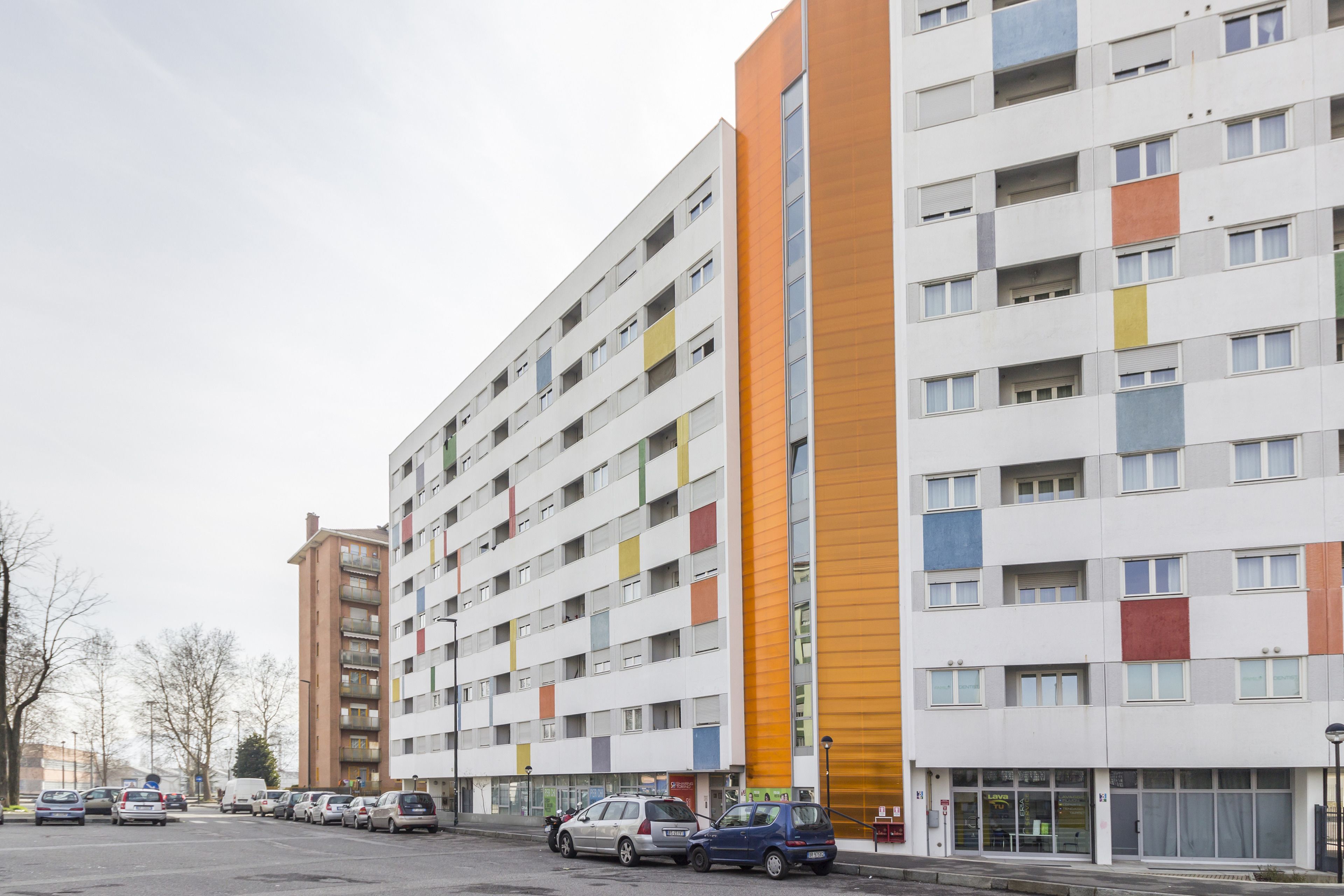 Um edifício residencial de vários andares com varandas, um estacionamento e um espaço comercial no térreo.