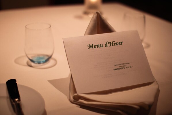 Um menu intitulado 'Menu d'Hiver' sobre uma mesa, com um copo e uma caneta.