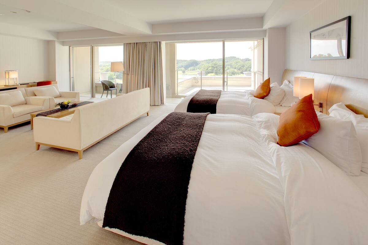 Quarto de hotel com duas camas, um sofá, uma escrivaninha e uma varanda com vista.
