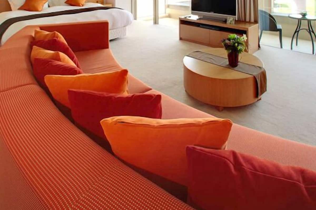 Quarto de hotel moderno com uma cama grande, um sofá, uma televisão e um espaço de refeições.