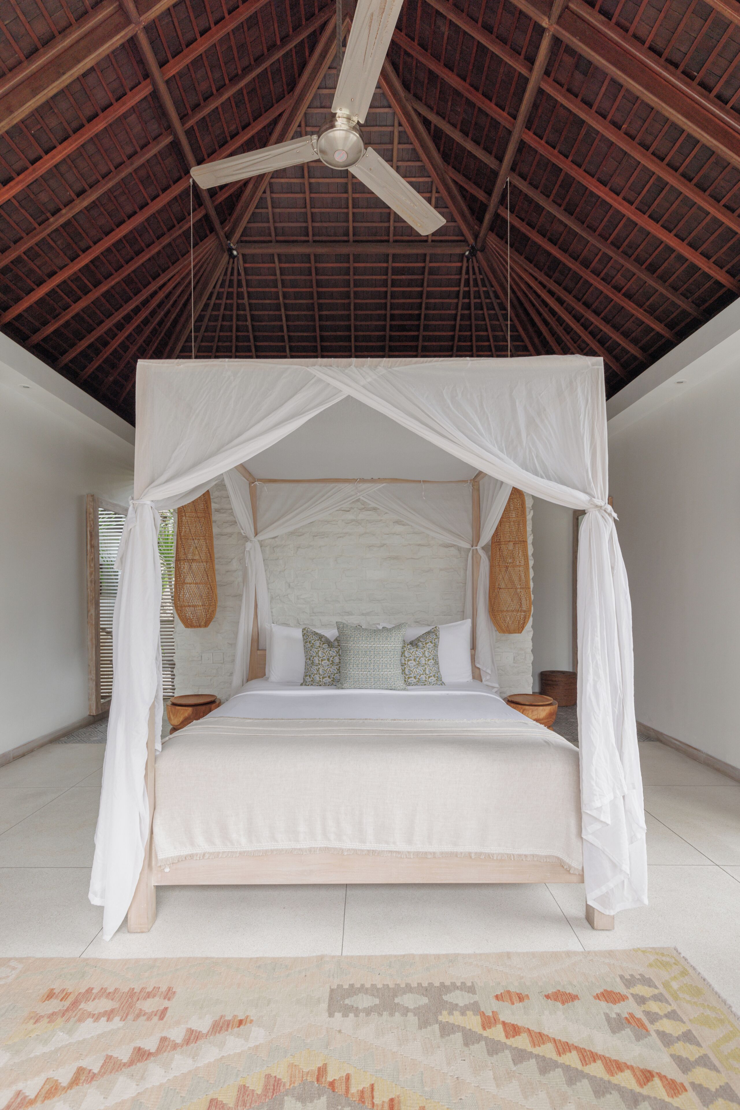 Quarto com cama de dossel, ventoinha no teto e tapete estampado.