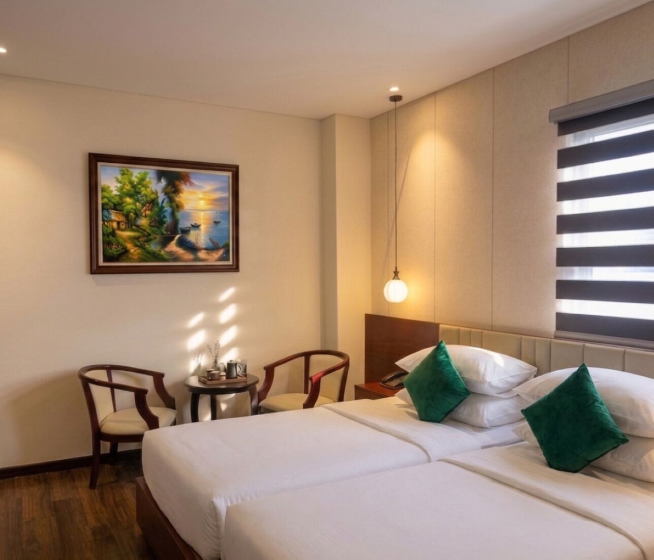 Quarto de hotel com uma cama, duas cadeiras, uma mesinha, um quadro e uma janela com persianas.