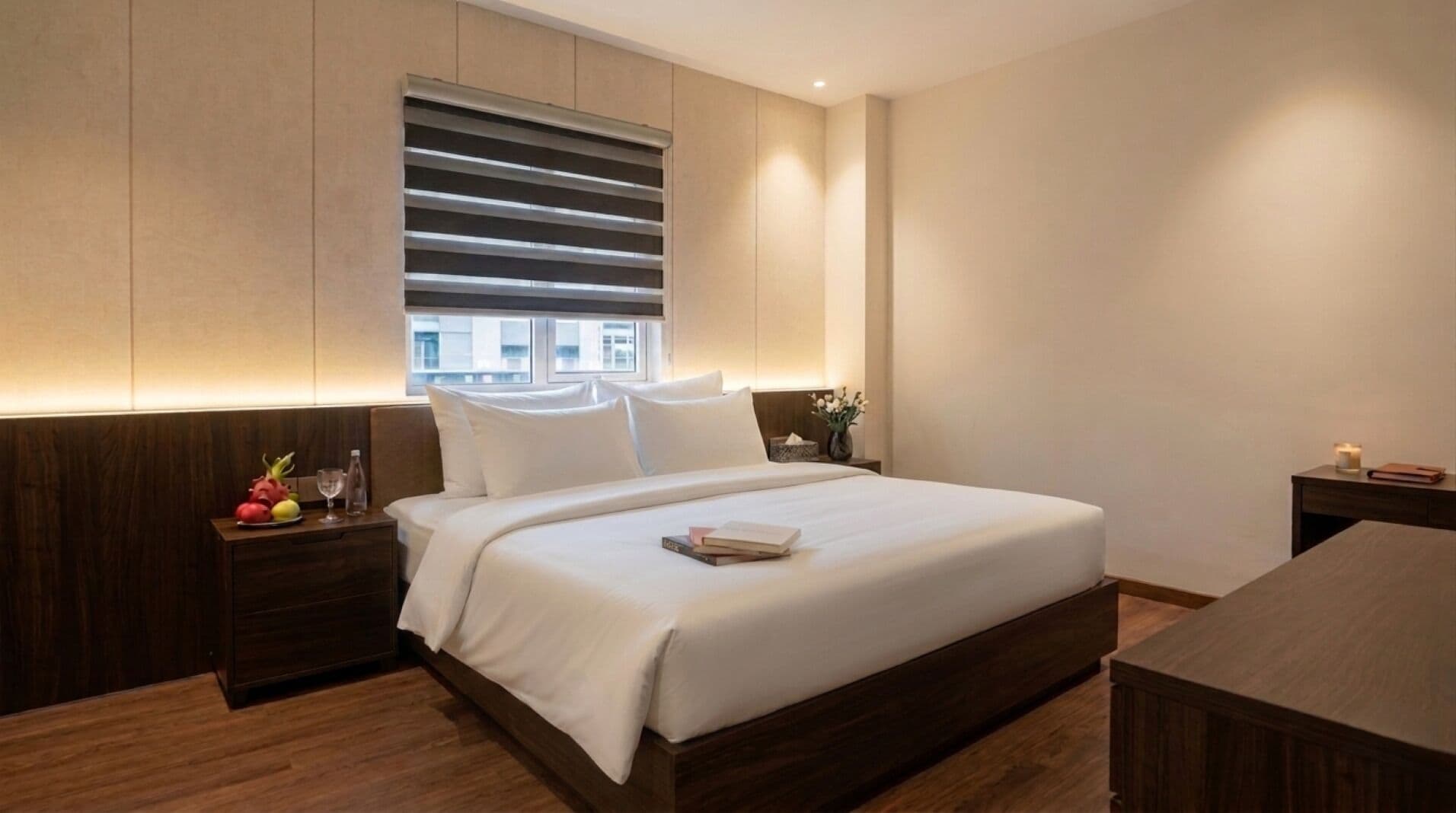 Quarto de hotel com uma cama grande, cabeceira de madeira, mesas de cabeceira, um criado-mudo, luminária e janela com persianas.