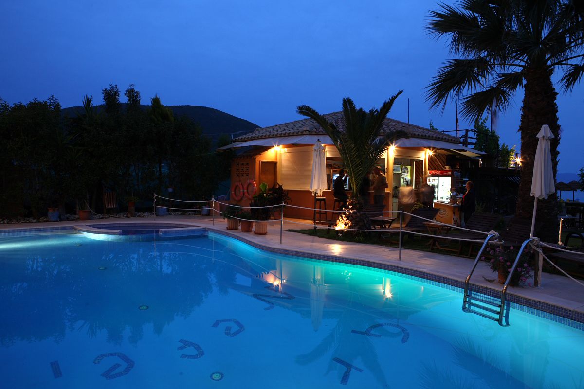 Piscina com área de bar, palmeiras e montanhas ao fundo.