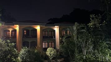 Um edifício grande e iluminado, com piscina e vegetação exuberante.