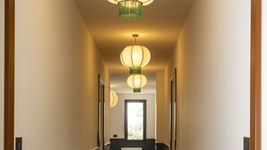 Um corredor com soalho de madeira, paredes verdes e iluminação pendente.
