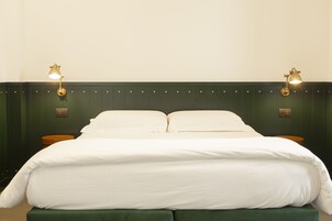 Cama bem arrumada com lençóis brancos, duas mesas de cabeceira com abajures e cabeceira verde.