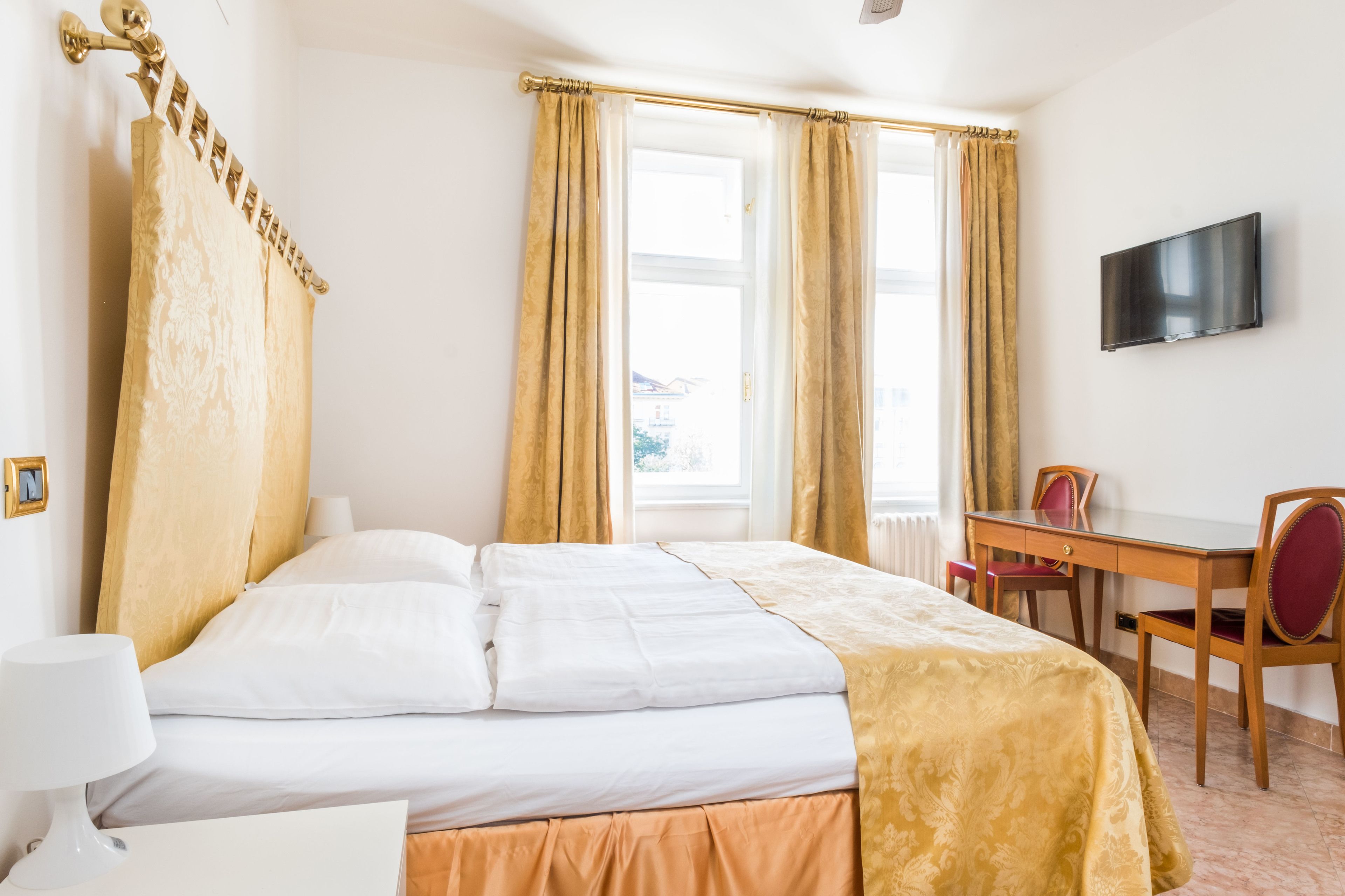 Quarto de hotel com cama, mesa de trabalho, cadeira, televisão e cortinas.