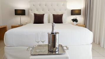 Cama bem arrumada com uma garrafa de champanhe e duas taças em um tabuleiro, cabeceira estofada e duas luminárias de mesa.