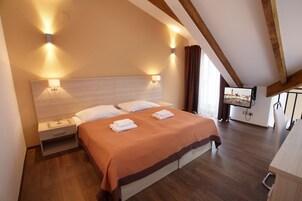 Quarto com cabeceira de madeira, cama com colcha laranja, duas mesas de cabeceira e uma TV de tela plana na parede.