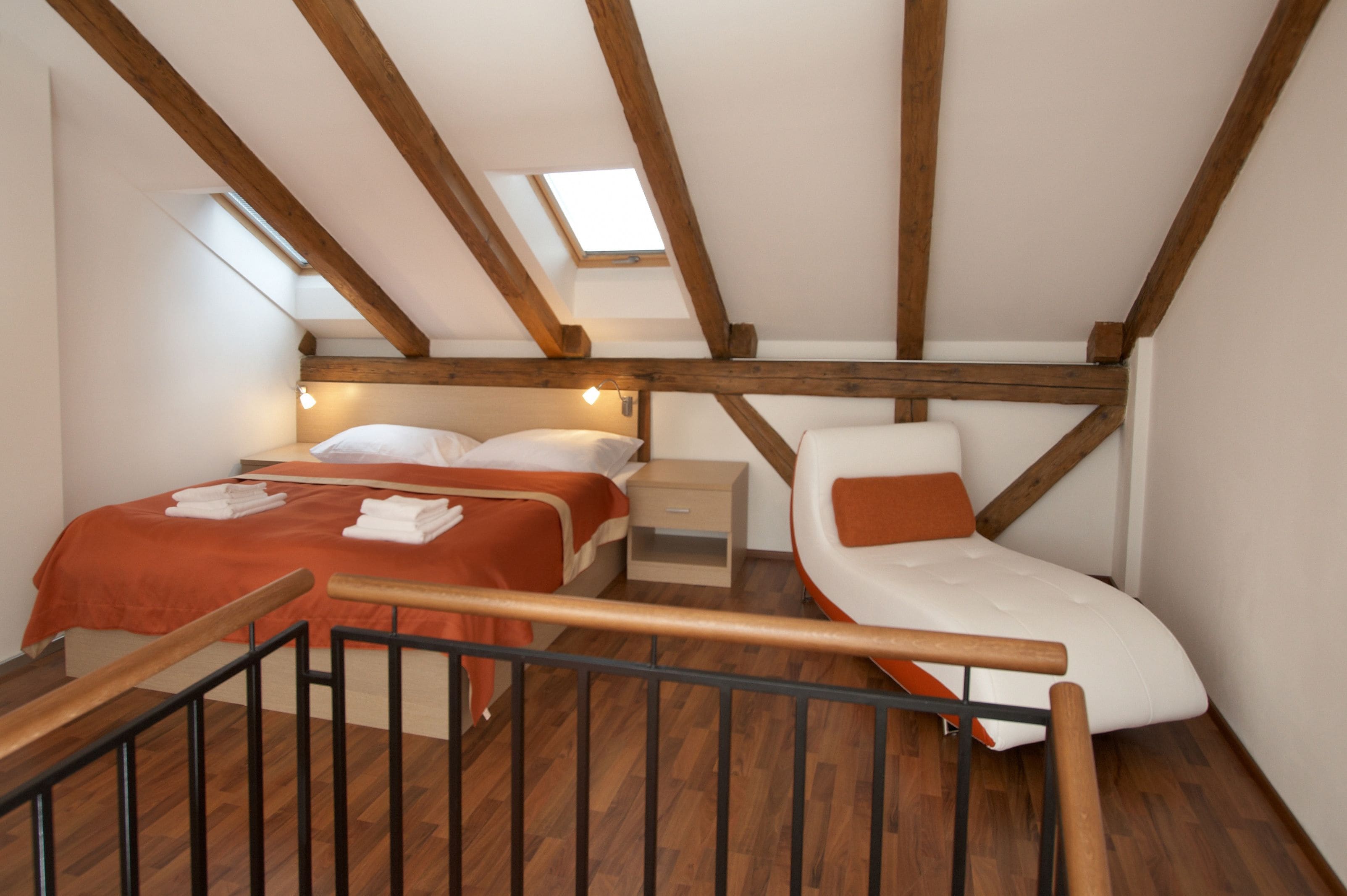 Quarto com teto estilo loft, vigas de madeira, cama, mesa de cabeceira e uma pequena mesa.