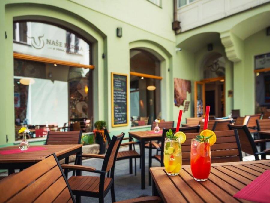 Uma área de refeições ao ar livre com mesas e cadeiras de madeira, um quadro de menu e o letreiro do restaurante.
