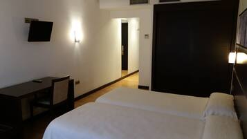Quarto de hotel com cama, escrivaninha e televisão na parede.