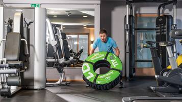 Academia com equipamentos de ginástica, um grande disco verde de exercício e uma esteira.