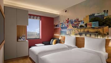Quarto de hotel com duas camas, uma parede de destaque vermelha, uma janela grande e um mural de paisagem urbana.