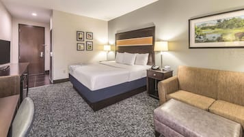Quarto de hotel com cama, mesas de cabeceira, escrivaninha, sofá e um quadro na parede.