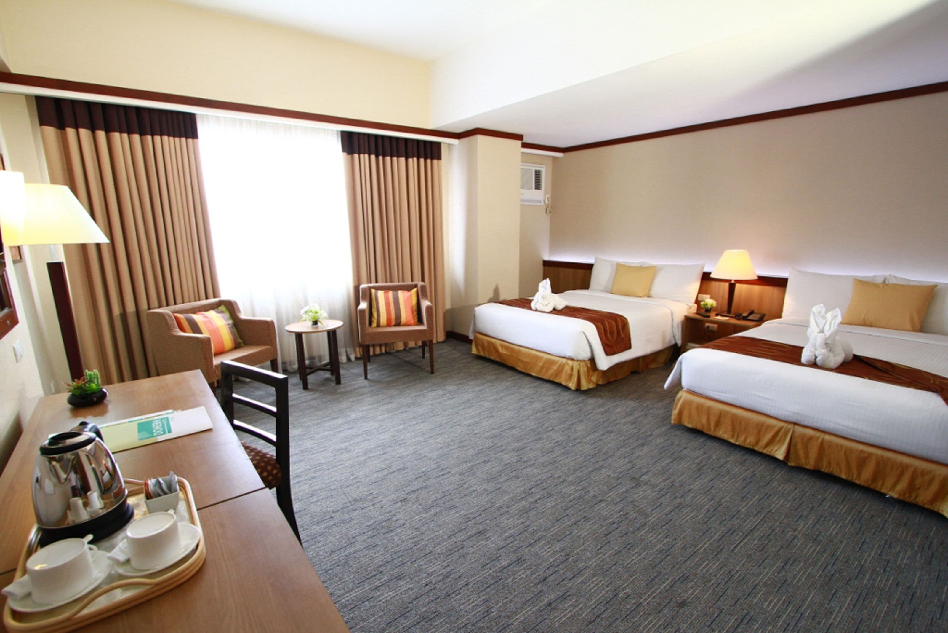 Quarto de hotel com duas camas, uma escrivaninha com uma bandeja de itens de café da manhã, uma cadeira e uma pequena mesa.