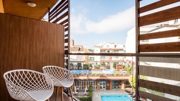 Varanda com duas cadeiras brancas, piscina e vista para edifícios e um restaurante.