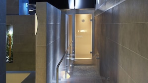 Escadaria interna moderna com corrimão de metal, que leva a uma porta com luminária acima.