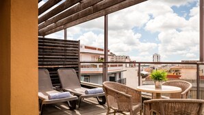Uma varanda com mobiliário de vime, uma mesa com um vaso e vista para a paisagem urbana.