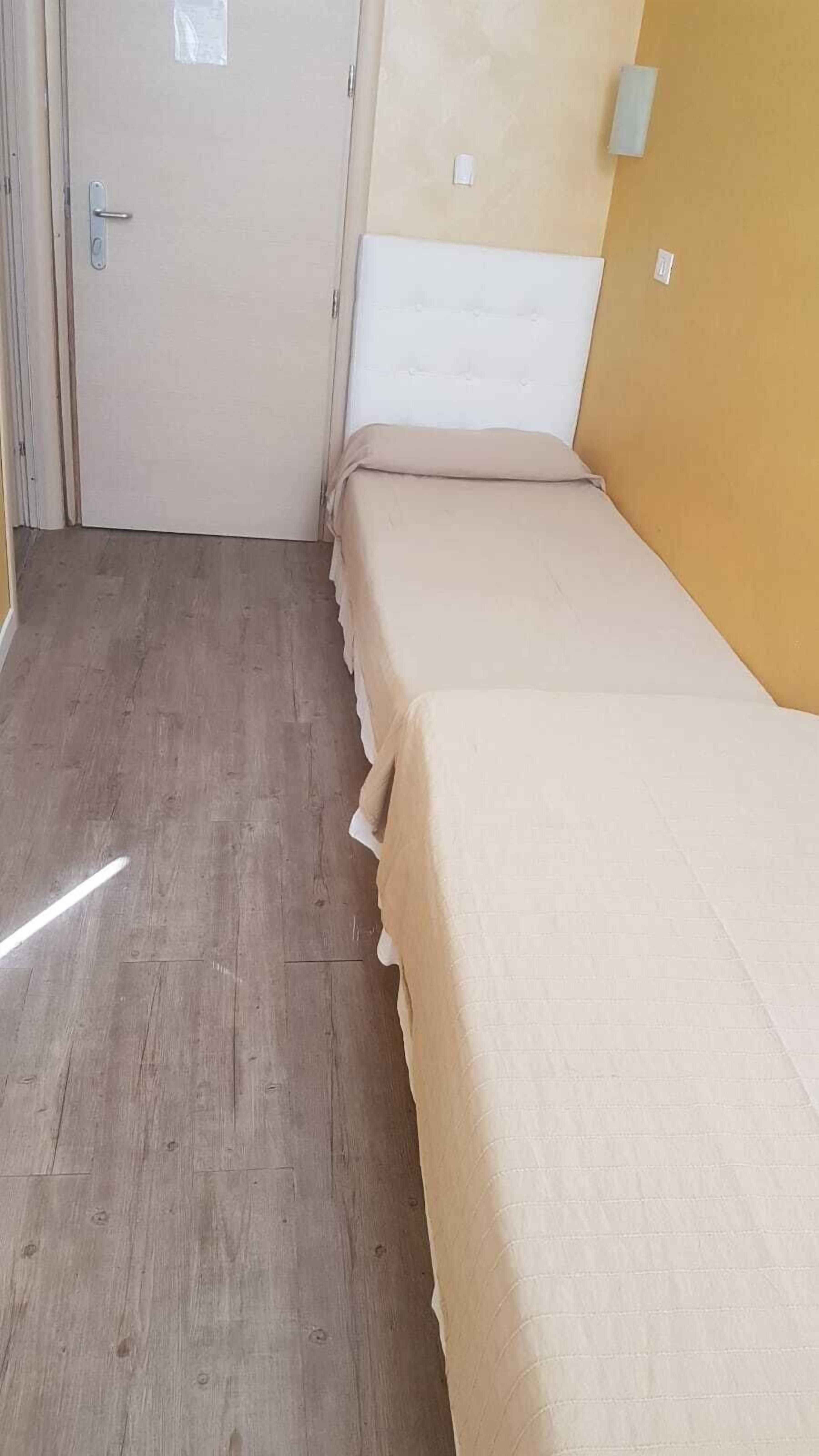 Um quarto com uma cama, uma porta e um candeeiro fixado na parede.