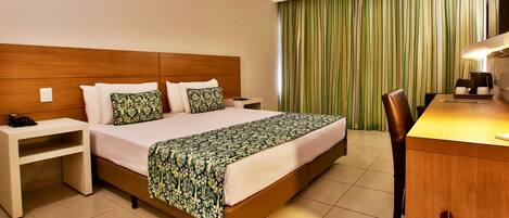 Quarto de hotel com uma cama, uma mesa, uma cadeira e uma cortina.