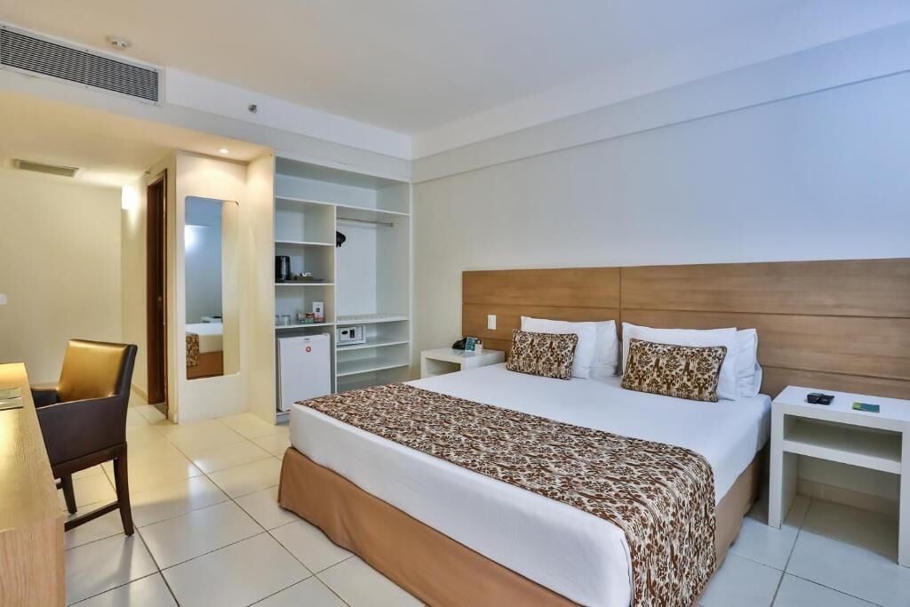 Quarto de hotel com uma cama grande, uma escrivaninha, uma cadeira e um guarda-roupa.
