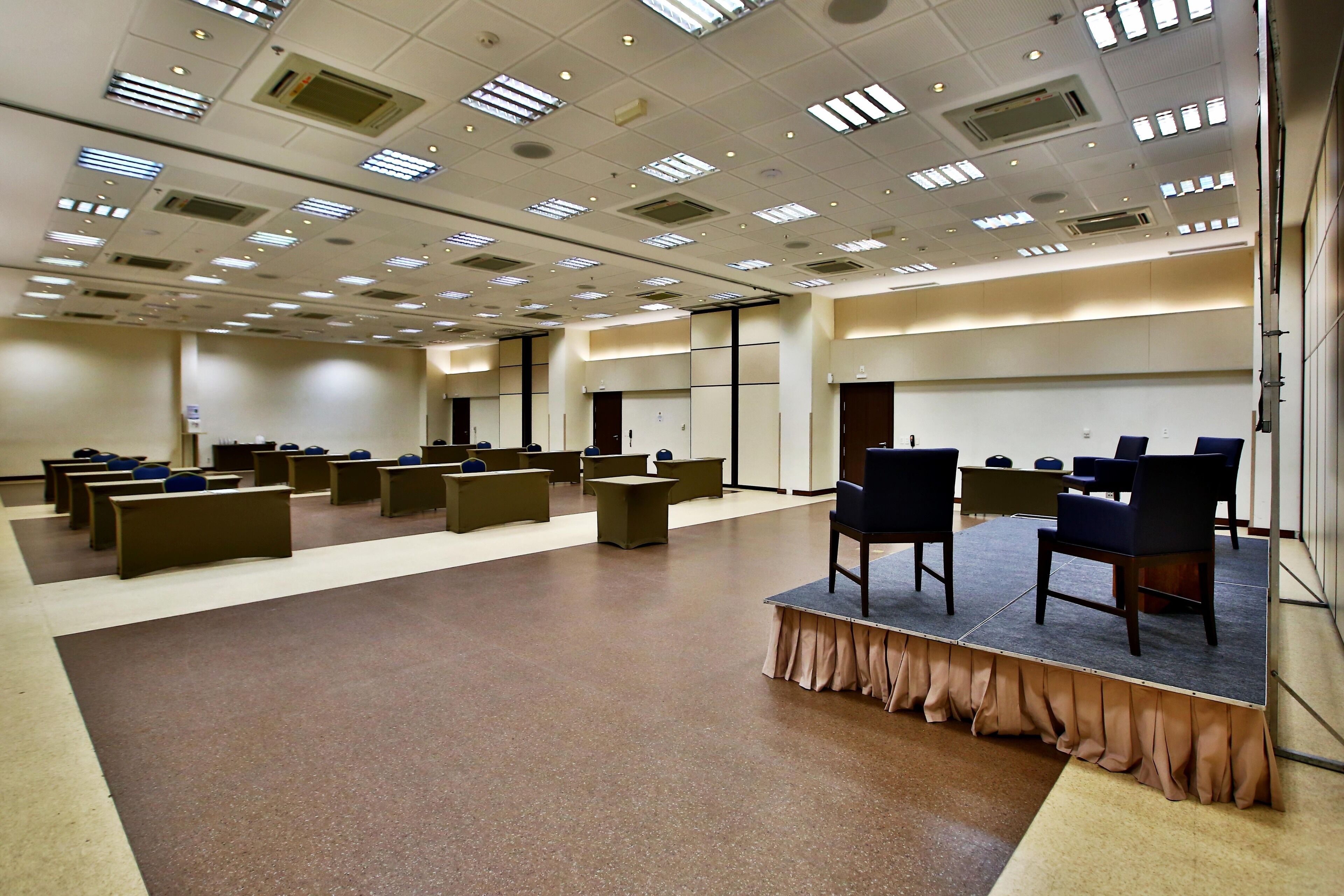 Uma sala de conferências com fileiras de cadeiras, um palco e uma tela grande.