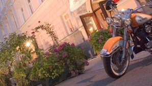 Entrada de hotel com fachada clássica, uma placa e uma motocicleta estacionada.