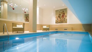 Uma piscina interior moderna com água azul cristalina, cadeiras de lounge em vime e um grande mural na parede.