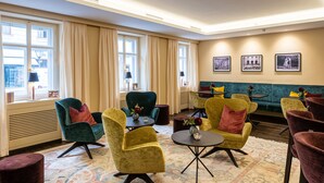 Um saguão de hotel com uma variedade de poltronas e sofás, um tapete estampado e uma parede com quadros emoldurados.