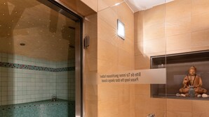 Uma área de spa moderna com uma banheira de hidromassagem em vidro, uma estátua de meditação e uma planta em vaso.