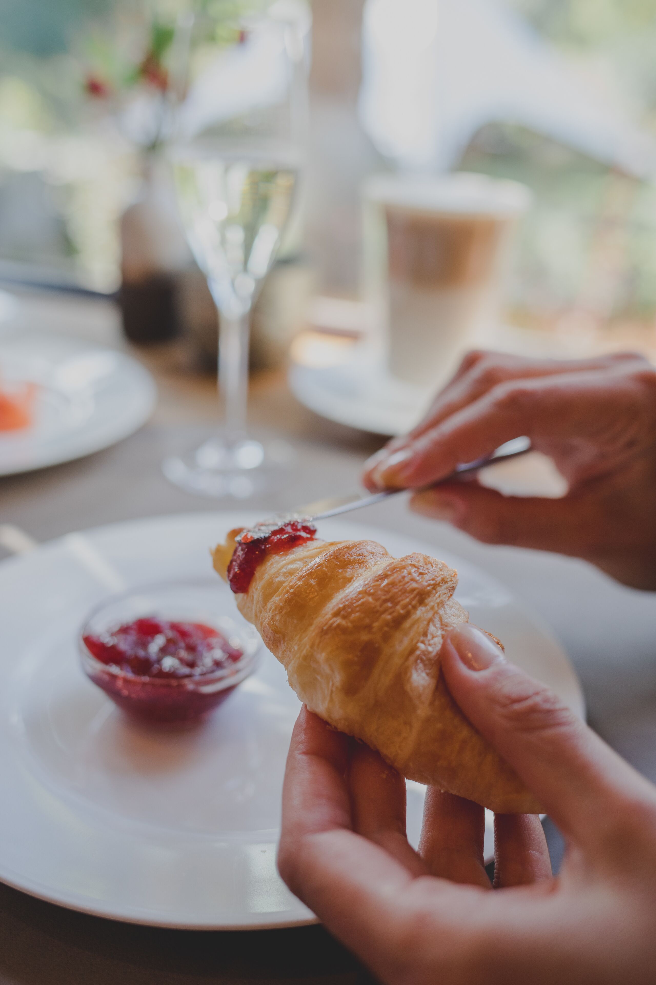 Uma pessoa segurando um croissant com geleia, com um prato de geleia e um copo de água ao fundo.