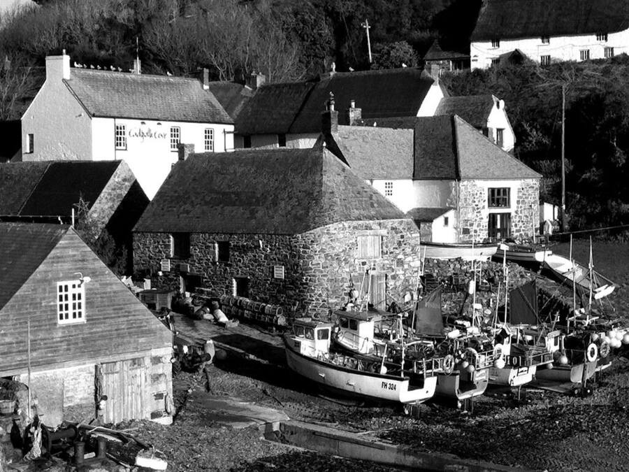 Uma vila costeira com edifícios de pedra, um cais com barcos e uma pequena igreja.