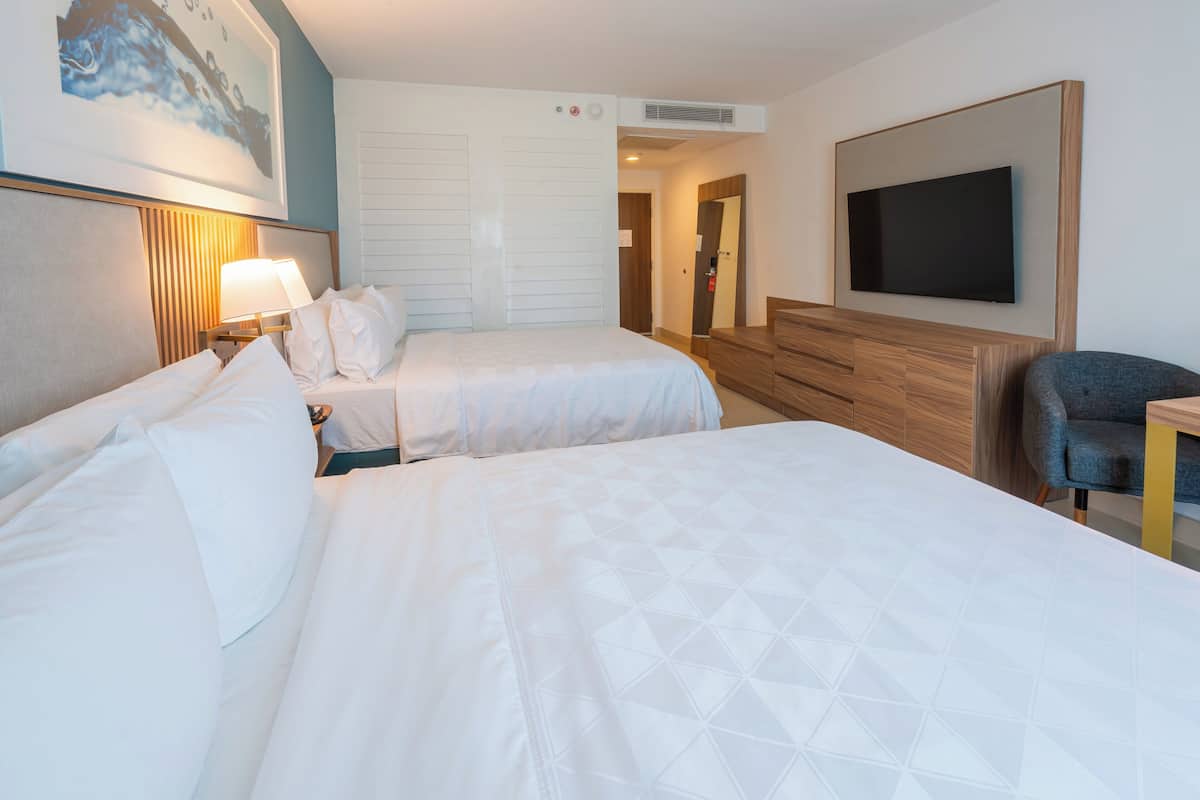 Quarto de hotel com duas camas, televisão, escrivaninha e uma cadeira.