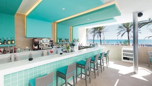 Uma área de bar com esquema de cores turquesa, banquetas e vista para a praia.