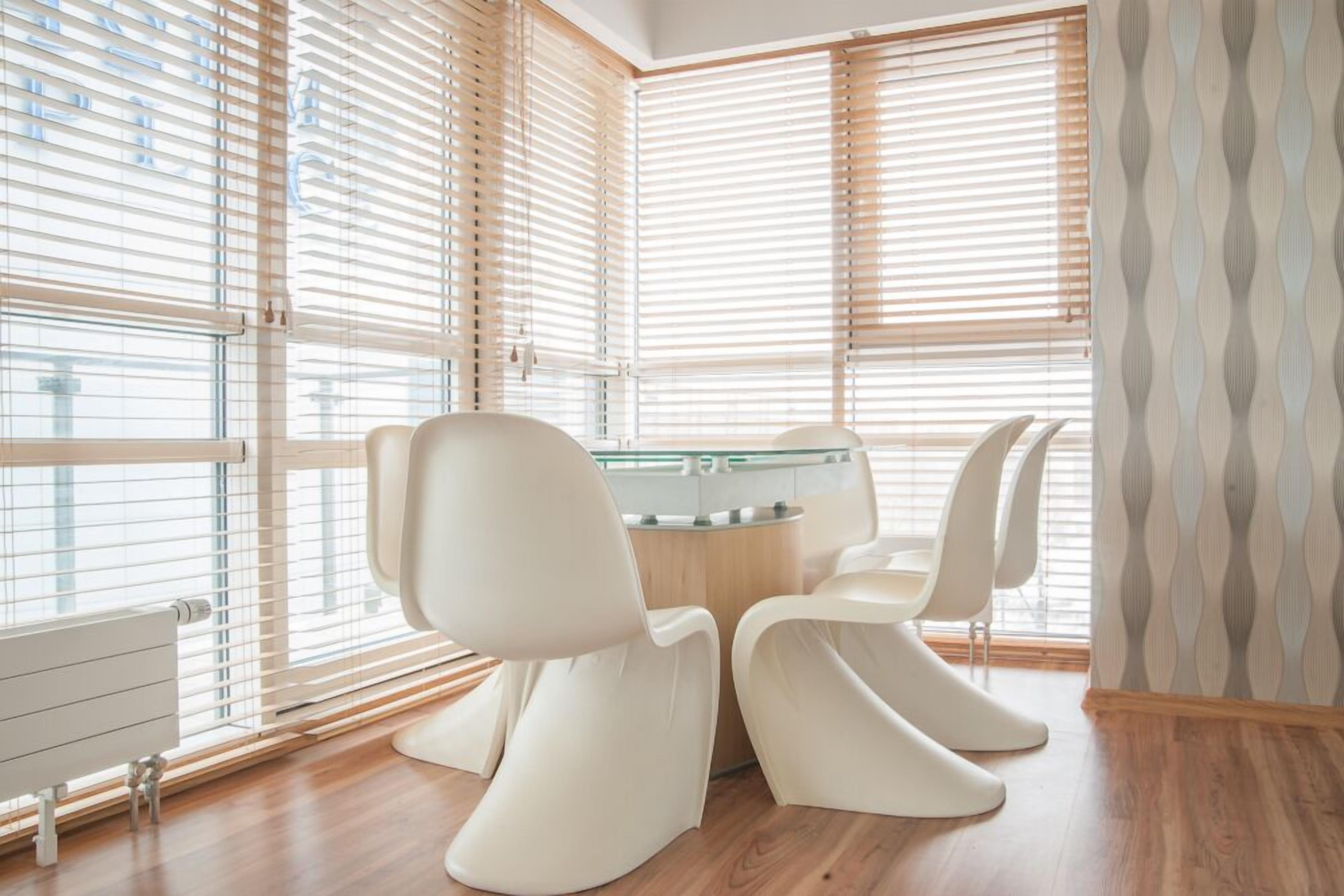 Quarto moderno com piso de madeira, cadeiras brancas e mesa de vidro.