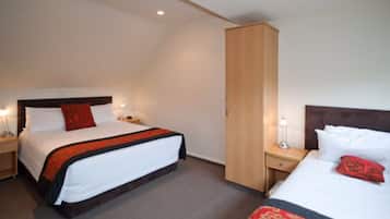 Quarto de hotel com duas camas, guarda-roupa, mesas de cabeceira com luminárias e chão coberto por carpete.