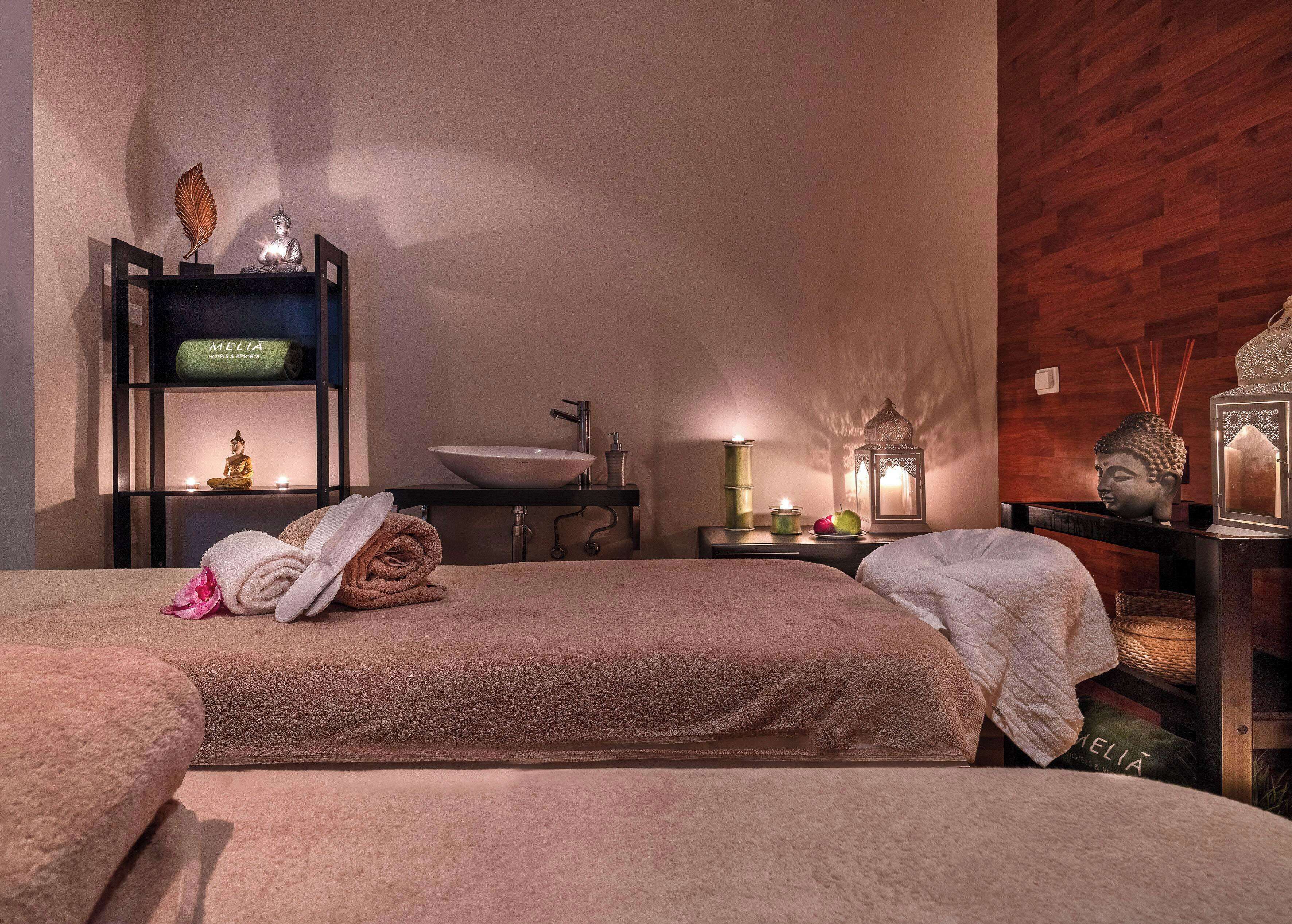 Uma sala de spa com duas camas, uma pia, uma estátua de Buda e uma prateleira com a cabeça de Buda e velas.