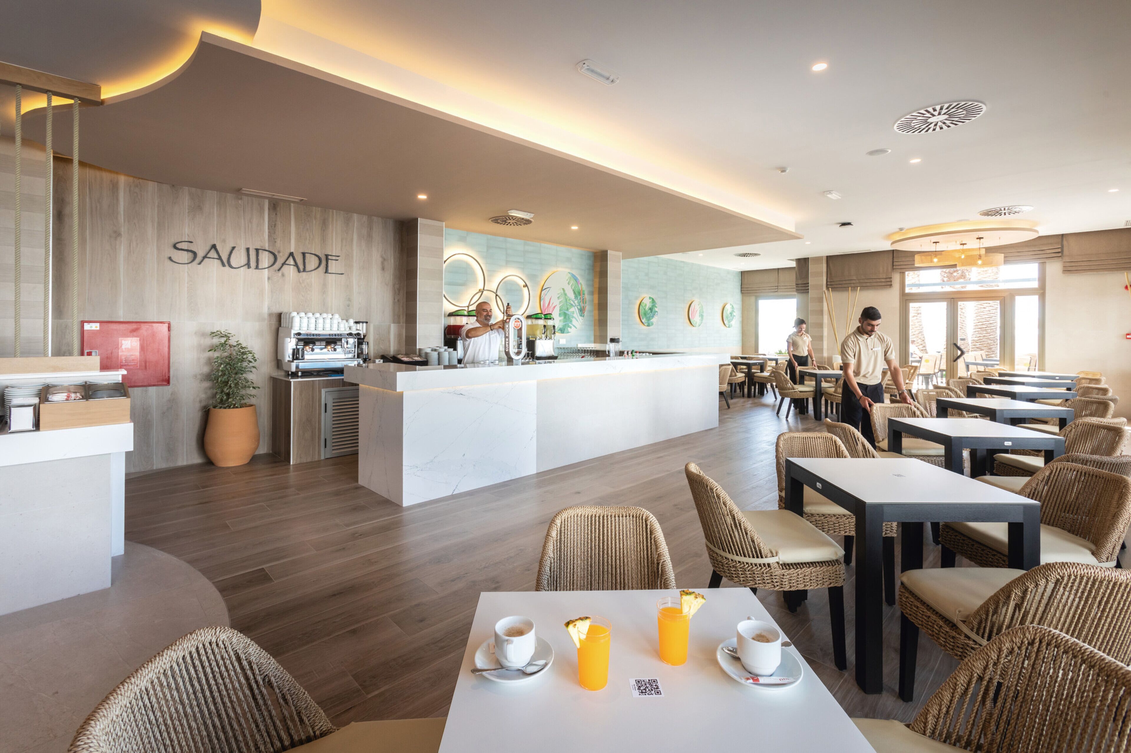 Um restaurante moderno com área de bar, piso de madeira e móveis de vime.