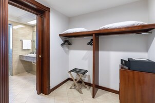 Quarto compacto com um banco de madeira, um banquinho pequeno e uma estante com roupas penduradas.