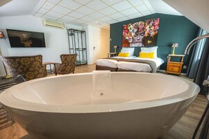 Quarto com uma banheira grande, cama com duas almofadas, televisão e um quadro na parede.