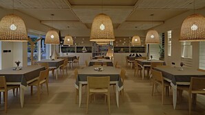 Uma sala de jantar ampla, com várias mesas e cadeiras, com luminárias pendentes feitas de fibra e uma paleta de cores neutras.