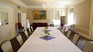 Uma sala de conferências com uma mesa comprida, cadeiras, um candelabro e um quadro na parede.