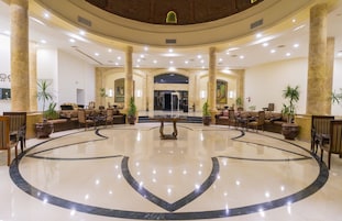 Um hall espaçoso com uma mesa redonda central, disposição de assentos e grandes colunas.