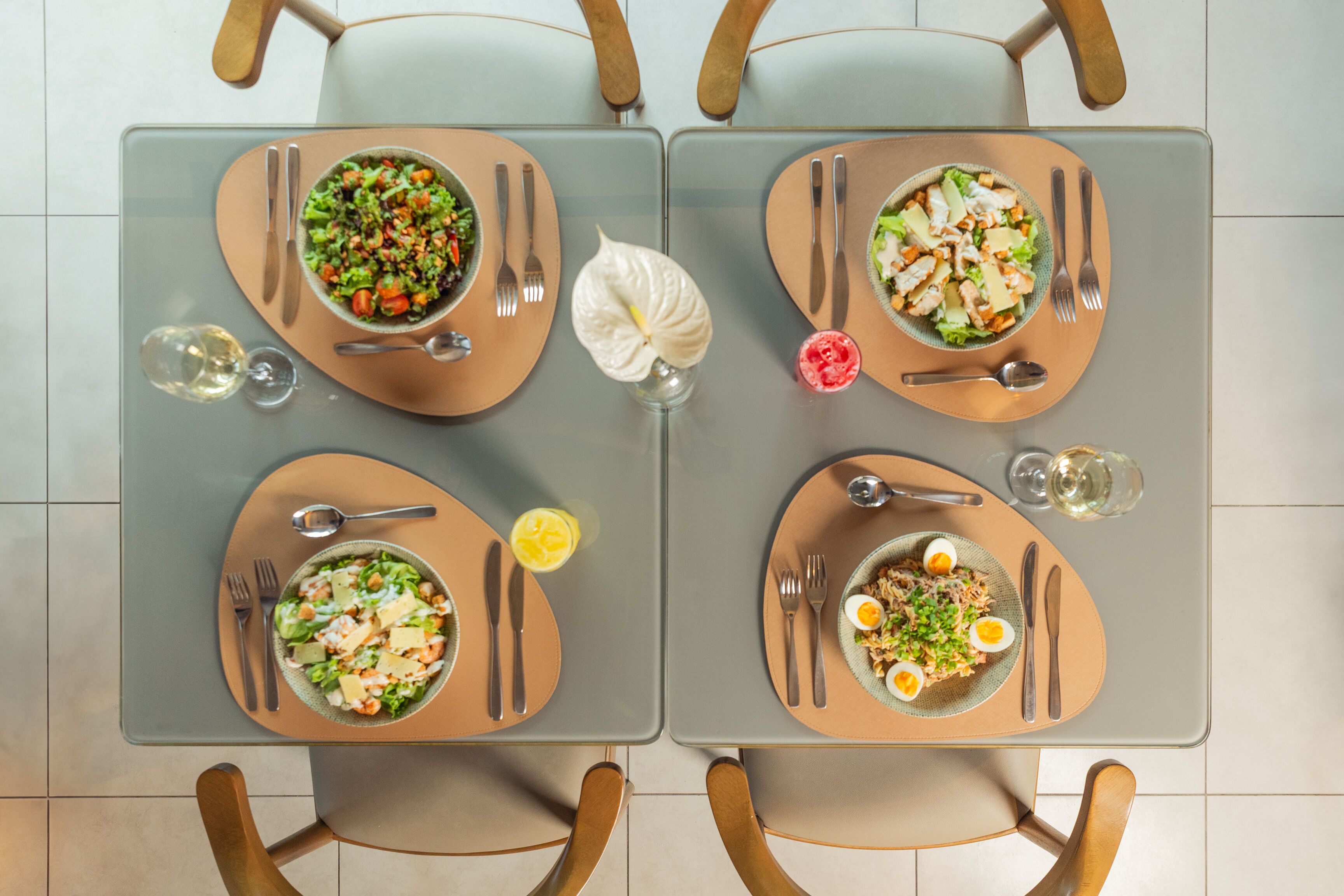 Uma mesa de jantar com quatro cadeiras, cada uma com um prato de comida, talheres e uma taça de vinho.