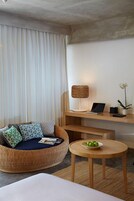 Quarto de hotel moderno com um sofá redondo de vime, uma escrivaninha de madeira com um laptop, uma pequena mesa redonda com uma tigela de maçãs e uma orquídea em vaso.