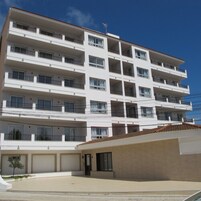 Um edifício residencial com vários andares, varandas, telhado plano e área de garagem.