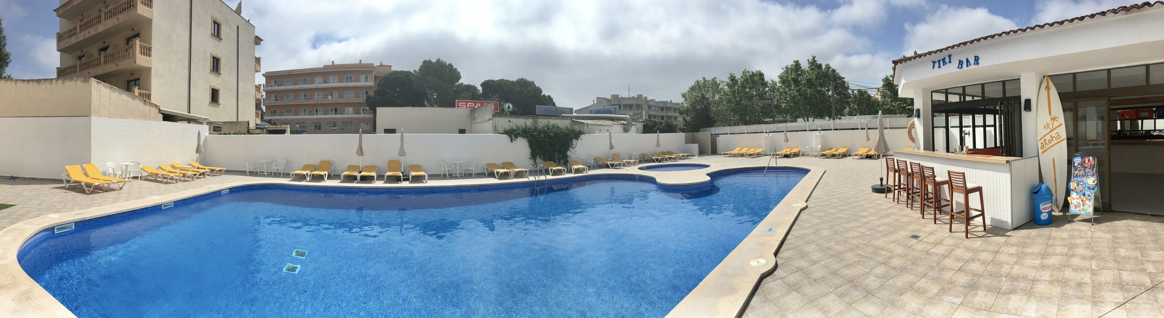 Piscina com cadeiras de sol amarelas e área de bar com uma prancha de surf.