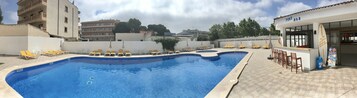 Piscina com cadeiras de sol amarelas e área de bar com uma prancha de surf.